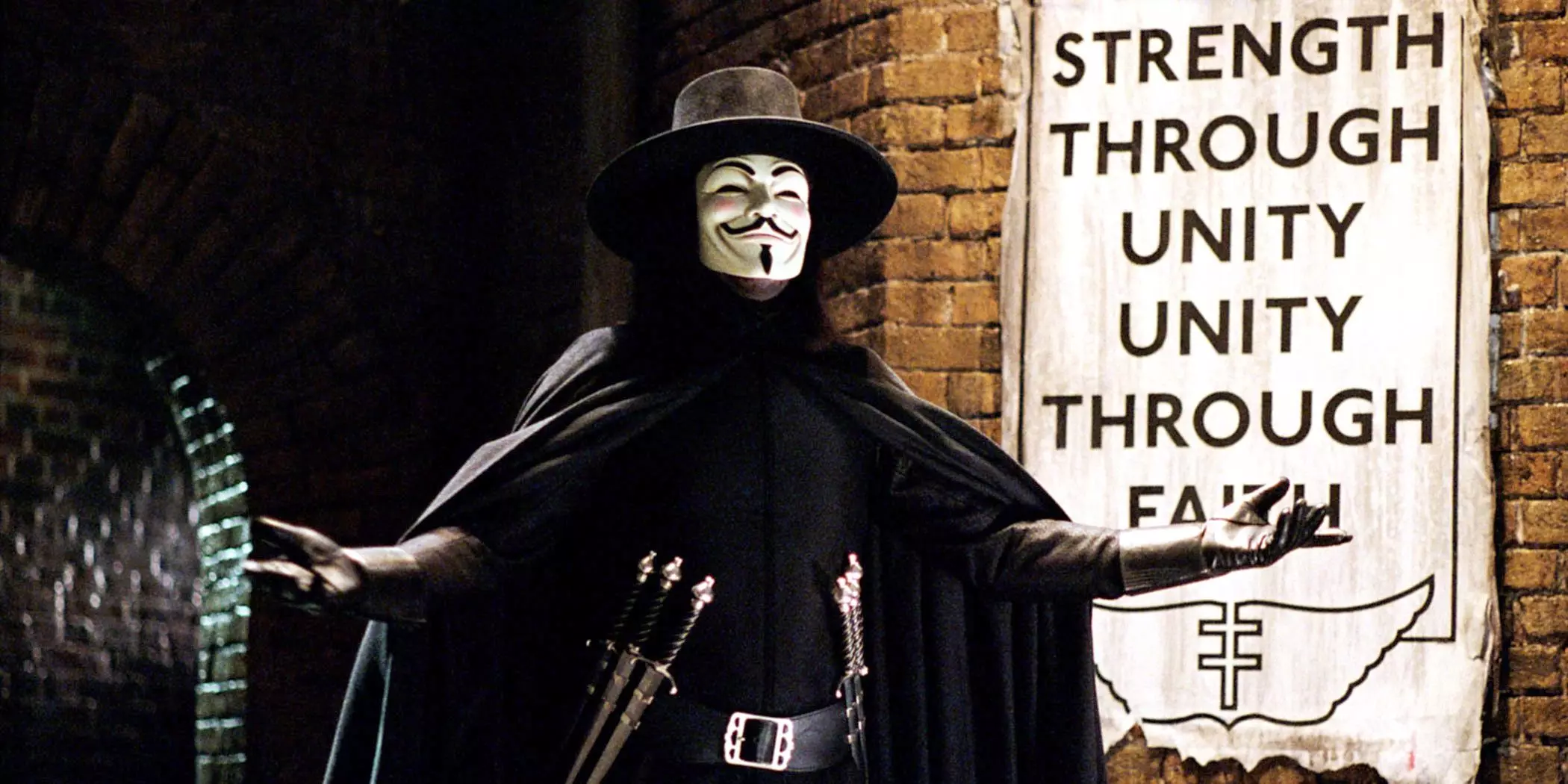 V, gespeeld door Hugo Weaving, gekleed in een Guy Fawkes-masker en met messen, staat in een steegje in V For Vendetta