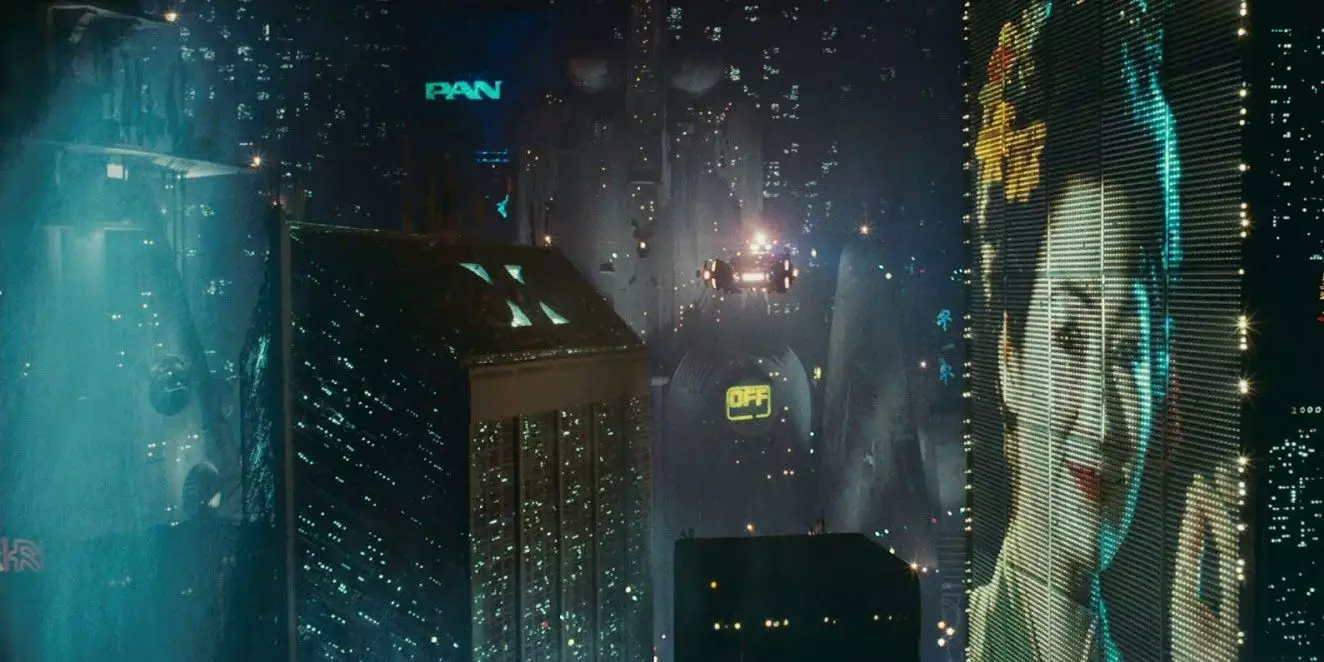 Een vliegende politieauto met Deckard erin vliegt door een rij wolkenkrabbers in het toekomstige Los Angeles, grote elektronische reclameborden op de gebouwen