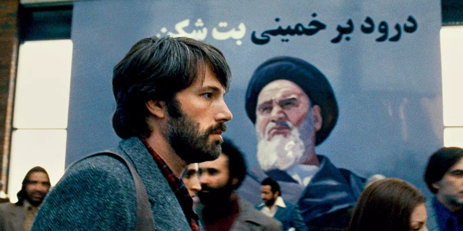 Ben Affleck als Tony Mendez langs een poster van de Iraanse ayatollah loopt in de film Argo