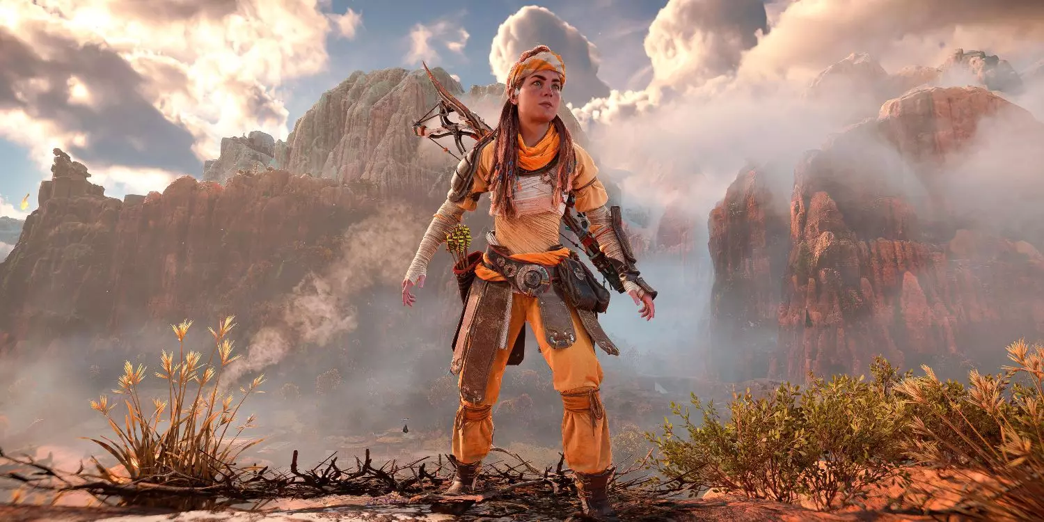 aloy dans une tenue ample jaune avec une ceinture utilitaire et un bandeau debout devant des montagnes brumeuses